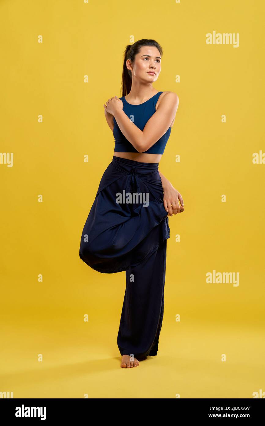 Graceful woman in black sportswear bending arm and leg, standing on ...