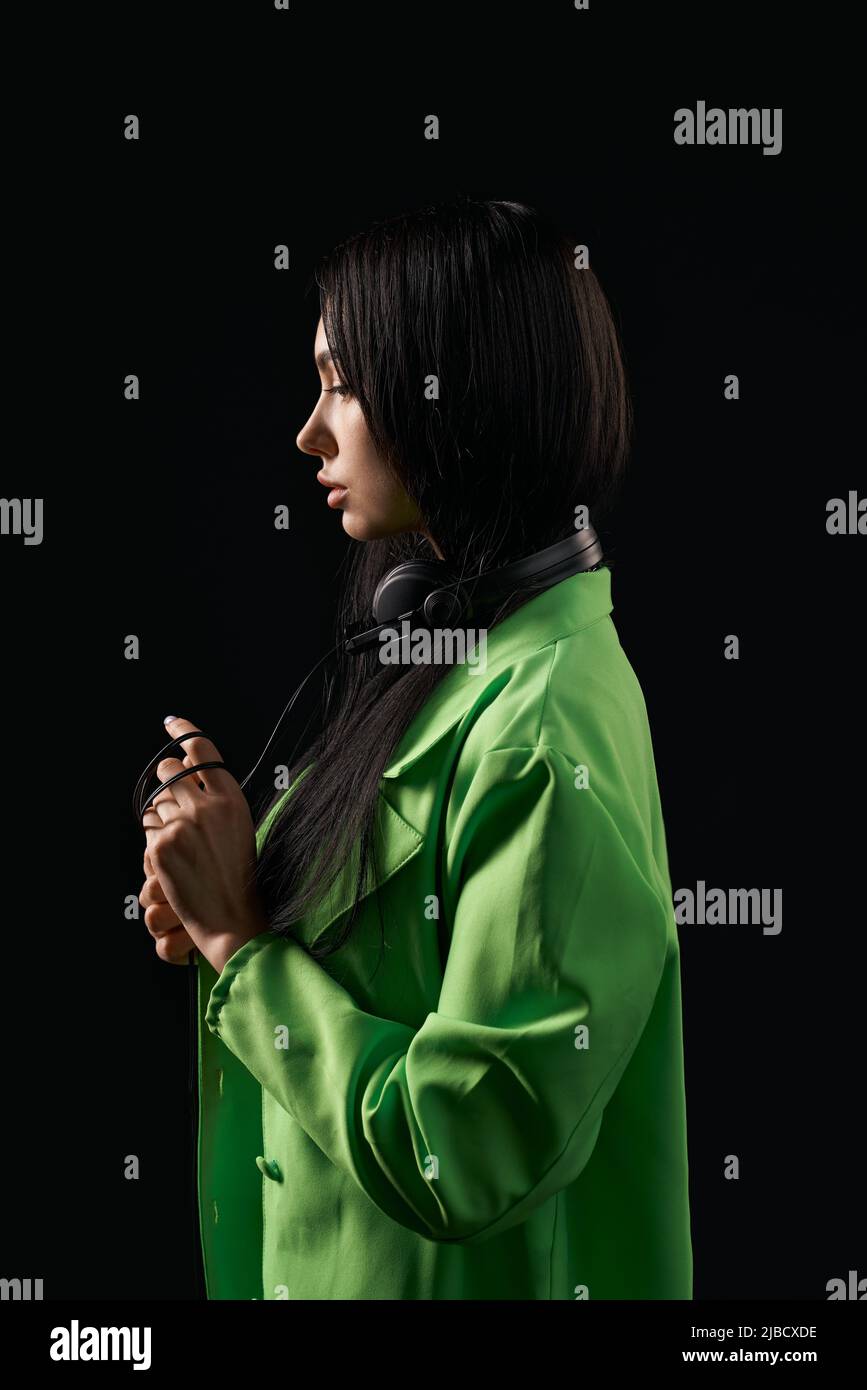 Thoughtful woman with headphones hanging on neck indoors. Side view of ...