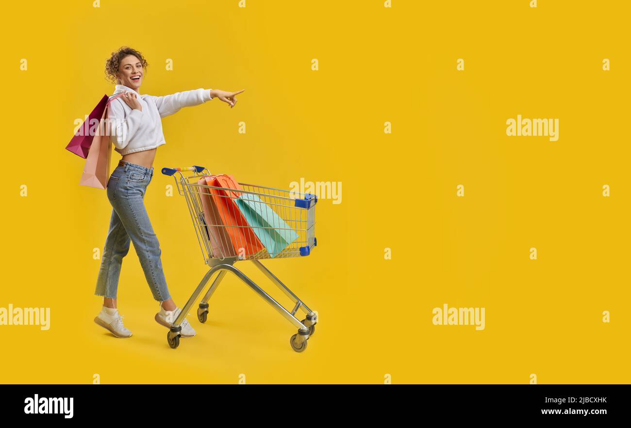 Beautiful female shopaholic pointing away, while shopping in studio ...