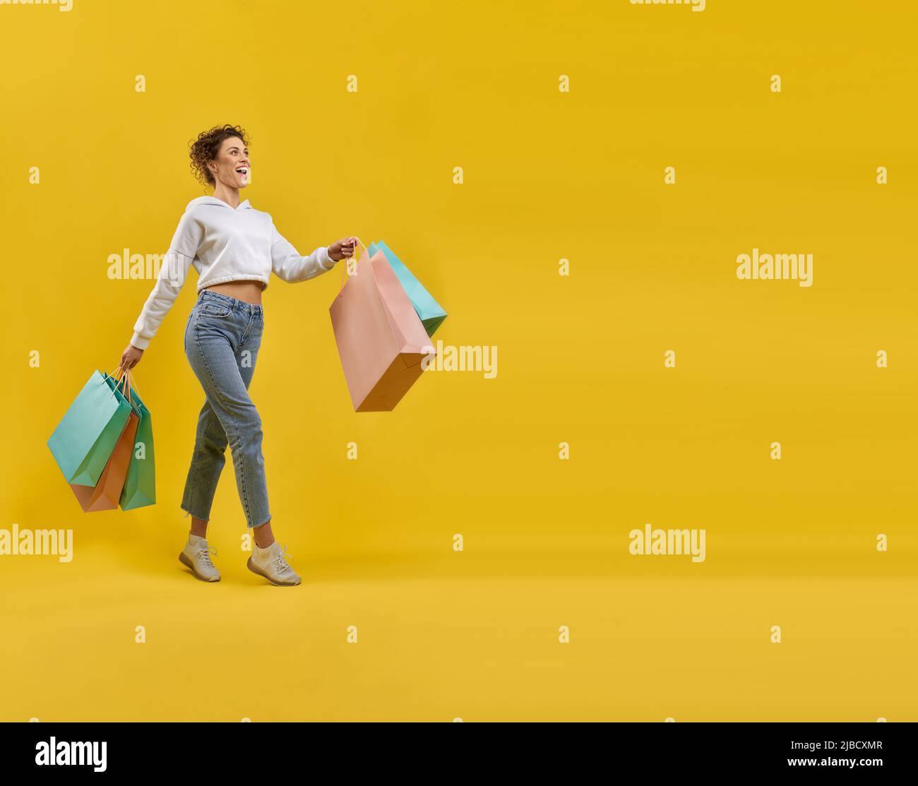 Delighted female shopper with paper bags walking alone after shopping ...
