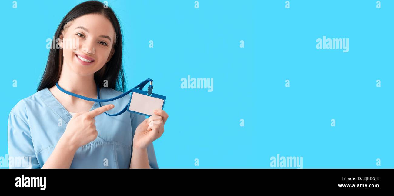 Female medical assistant pointing at her badge on light blue background ...