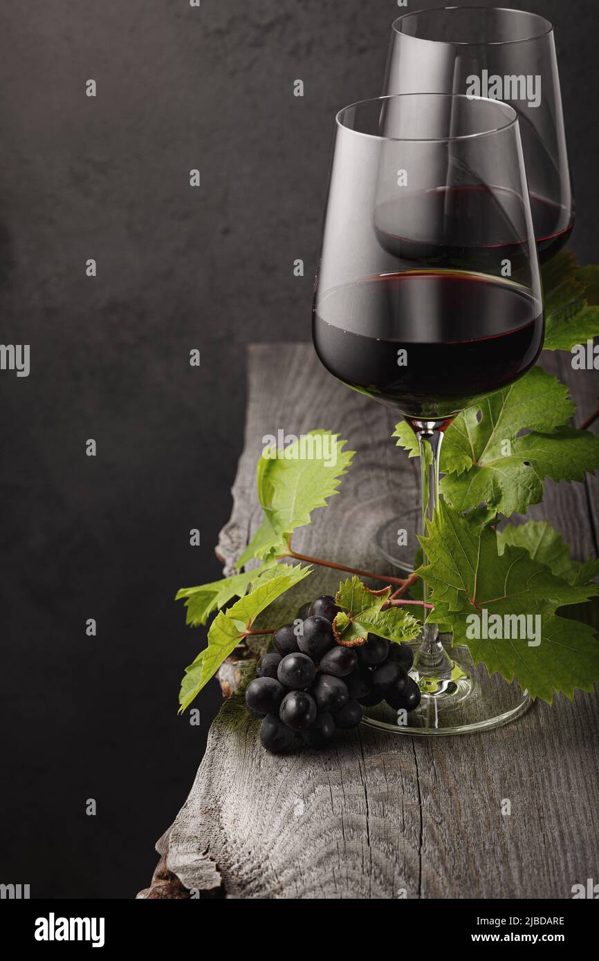 Two glasses of red wine, grapes and grape leaves on an old wooden table ...