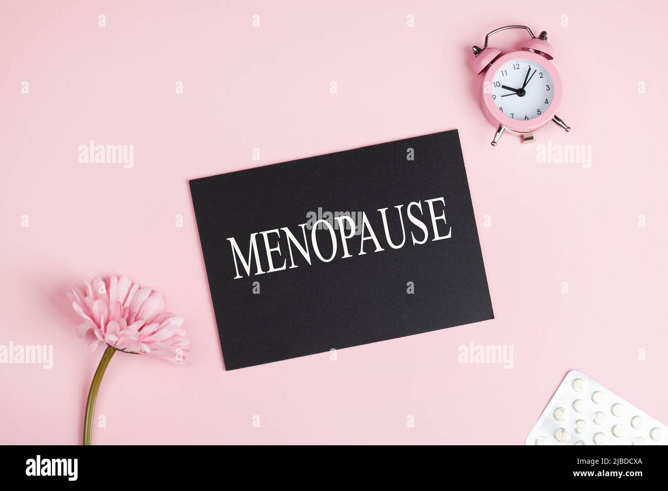 menopause word written on black board, flowers, clock and pills on pink ...