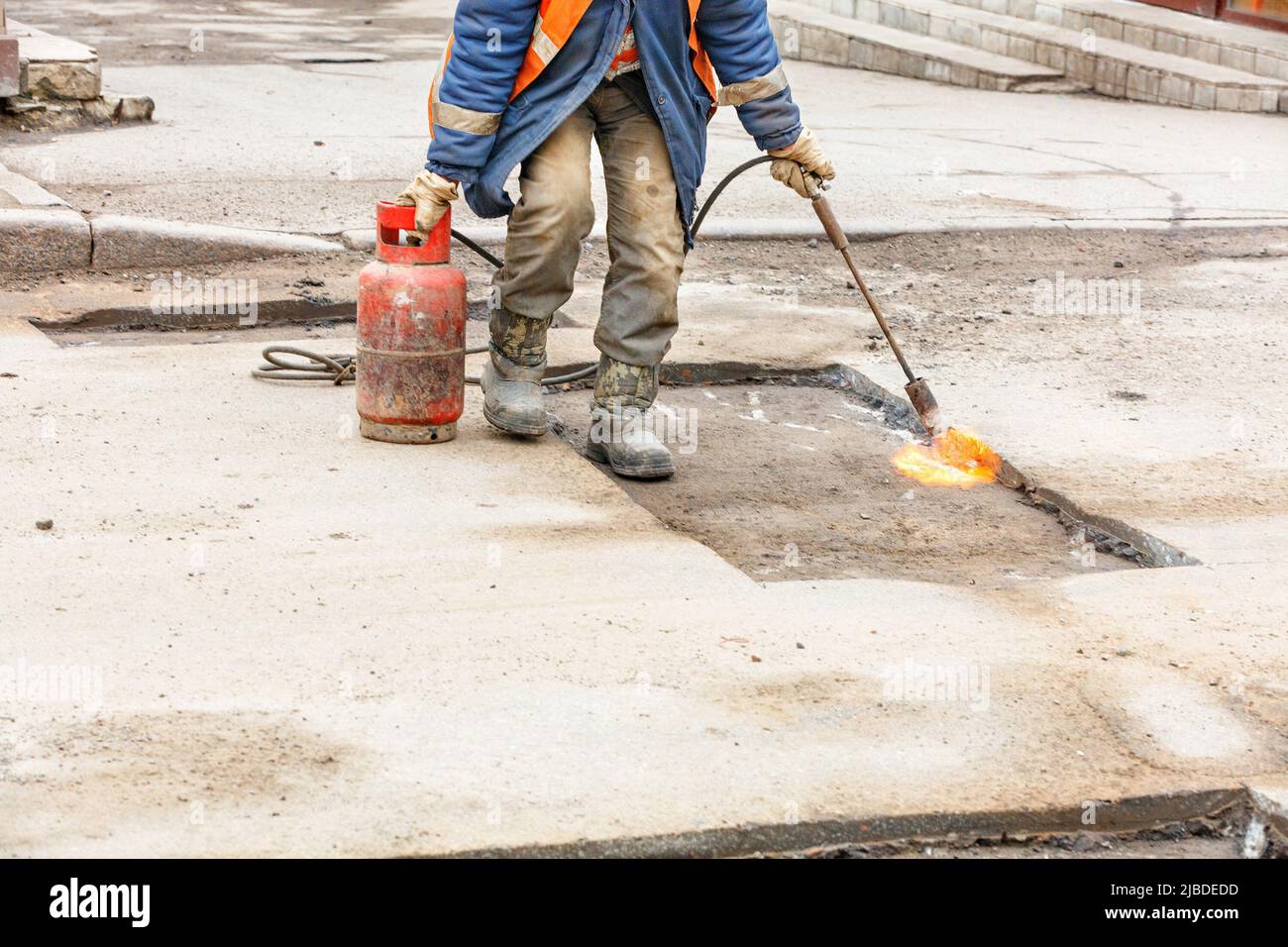 A worker using a gas burner heats the asphalt pavement for patching the ...