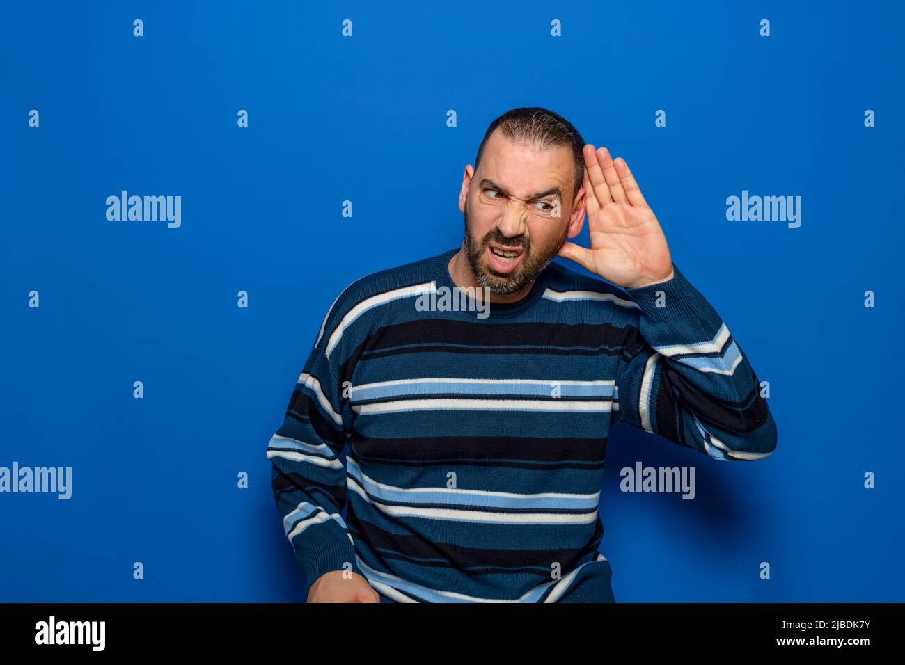 Listening male holds his hand near his ear over blue background ...