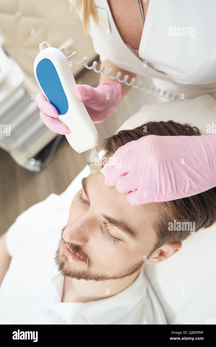 Beautician operating ultrasonic skin scrubber while cleaning man ...