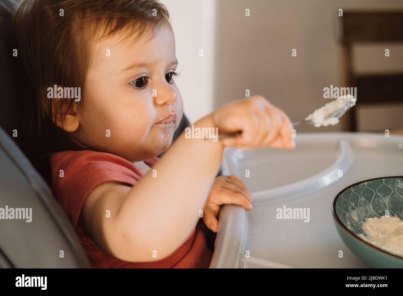Baby try eating the oatmeal with a spoon from a bowl. Little boy ...