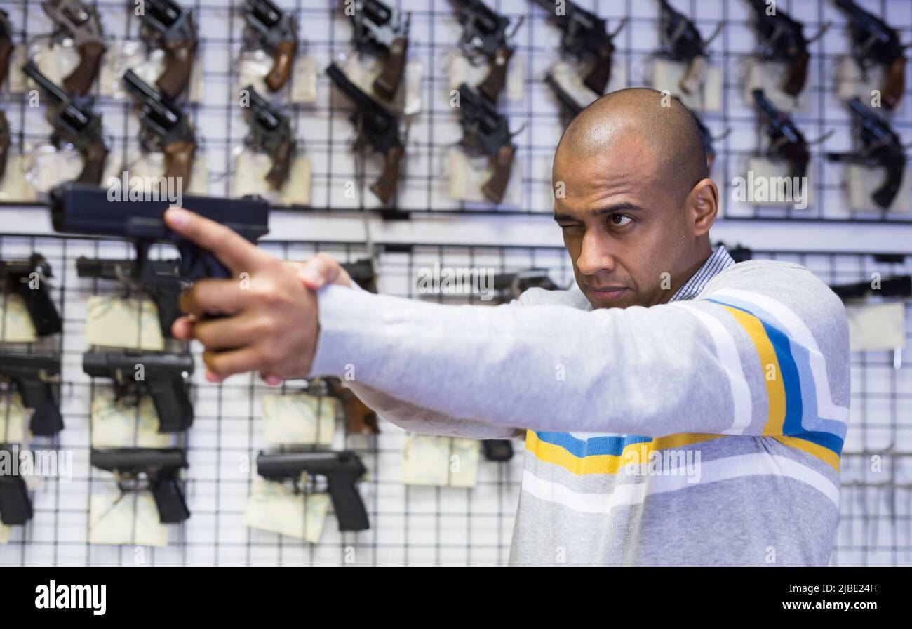 Focused latin american man aiming with pistol in gun shop Stock Photo ...