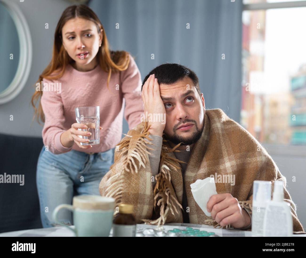Man with cold symptoms sitting at home while girlfriend caring him ...