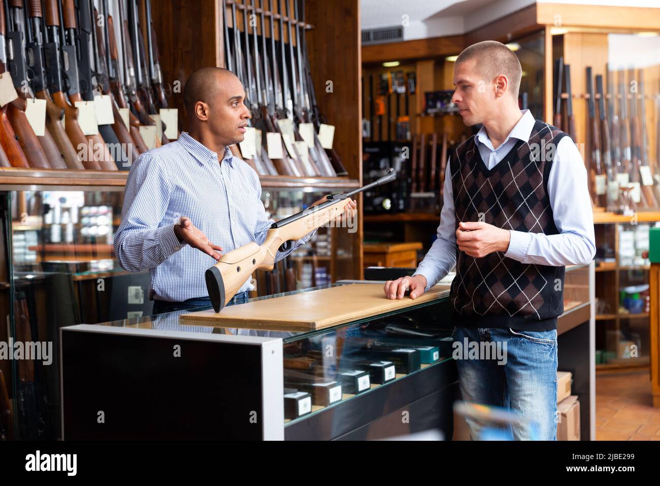 Latin american man owner of gun shop consulting customer about rifle ...