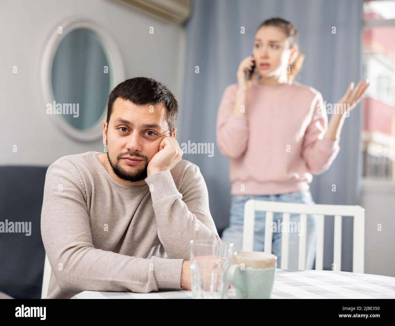 Offended man sitting at table while girlfriend talking on phone Stock ...