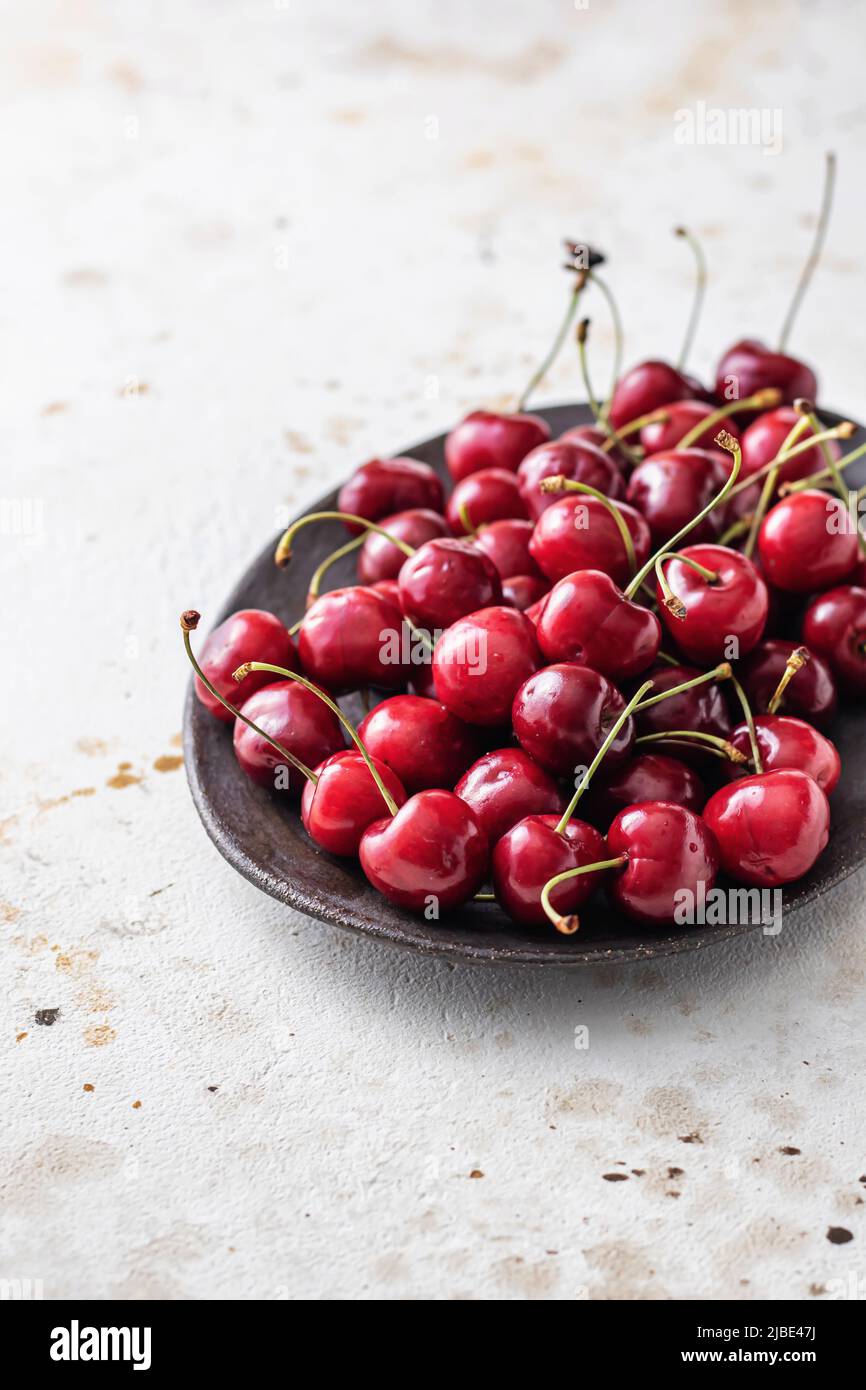 Fresh cherries in brown oval plate on white textured background, copy ...