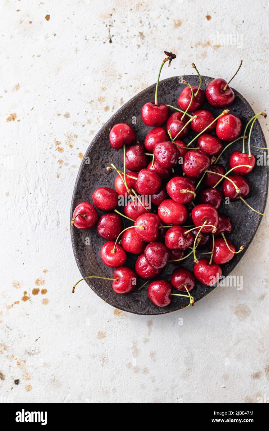 Fresh cherries in a brown oval plate on white textured background, top ...
