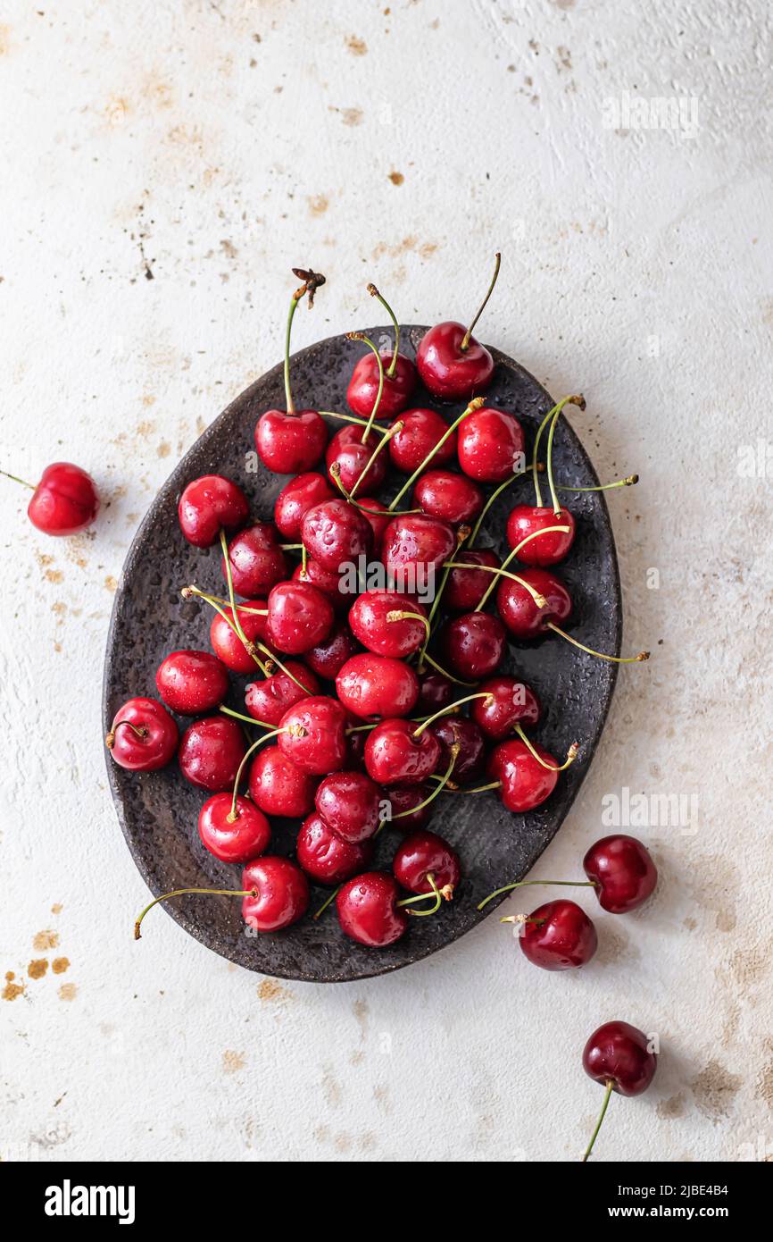 Fresh cherries in a brown oval plate on white textured background, top ...