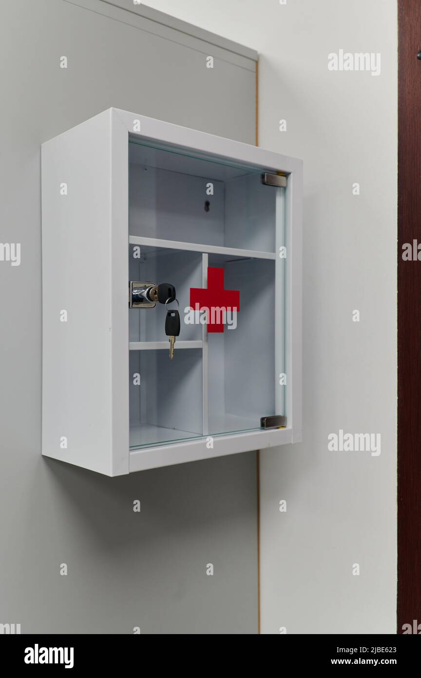 wall-mounted metal first-aid kit with a red cross on the glass in the ...