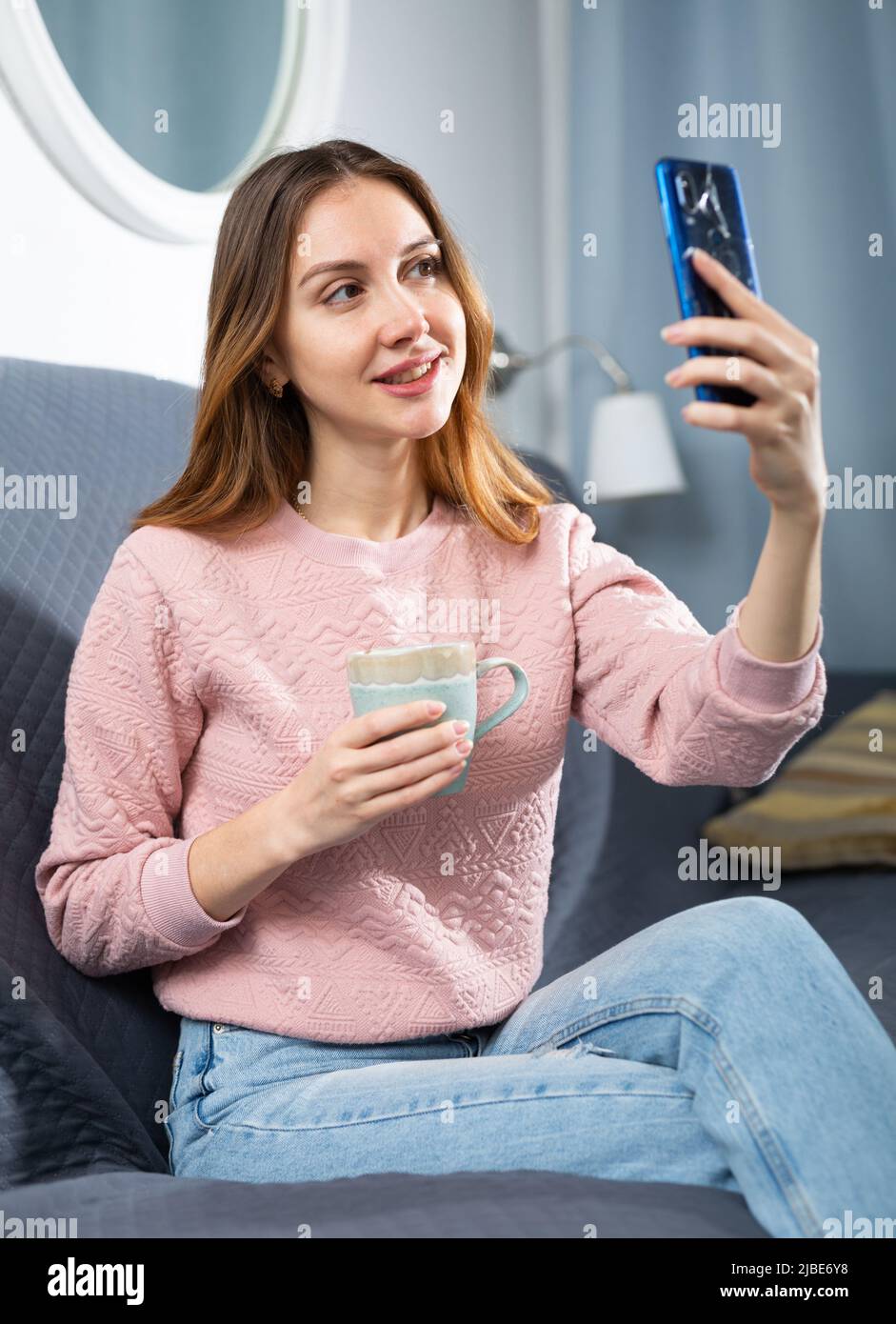 Smiling young woman using phone at home Stock Photo - Alamy