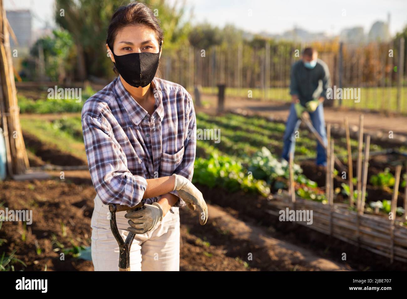 Young woman gardener holding shovel in garden with mask for protect ...
