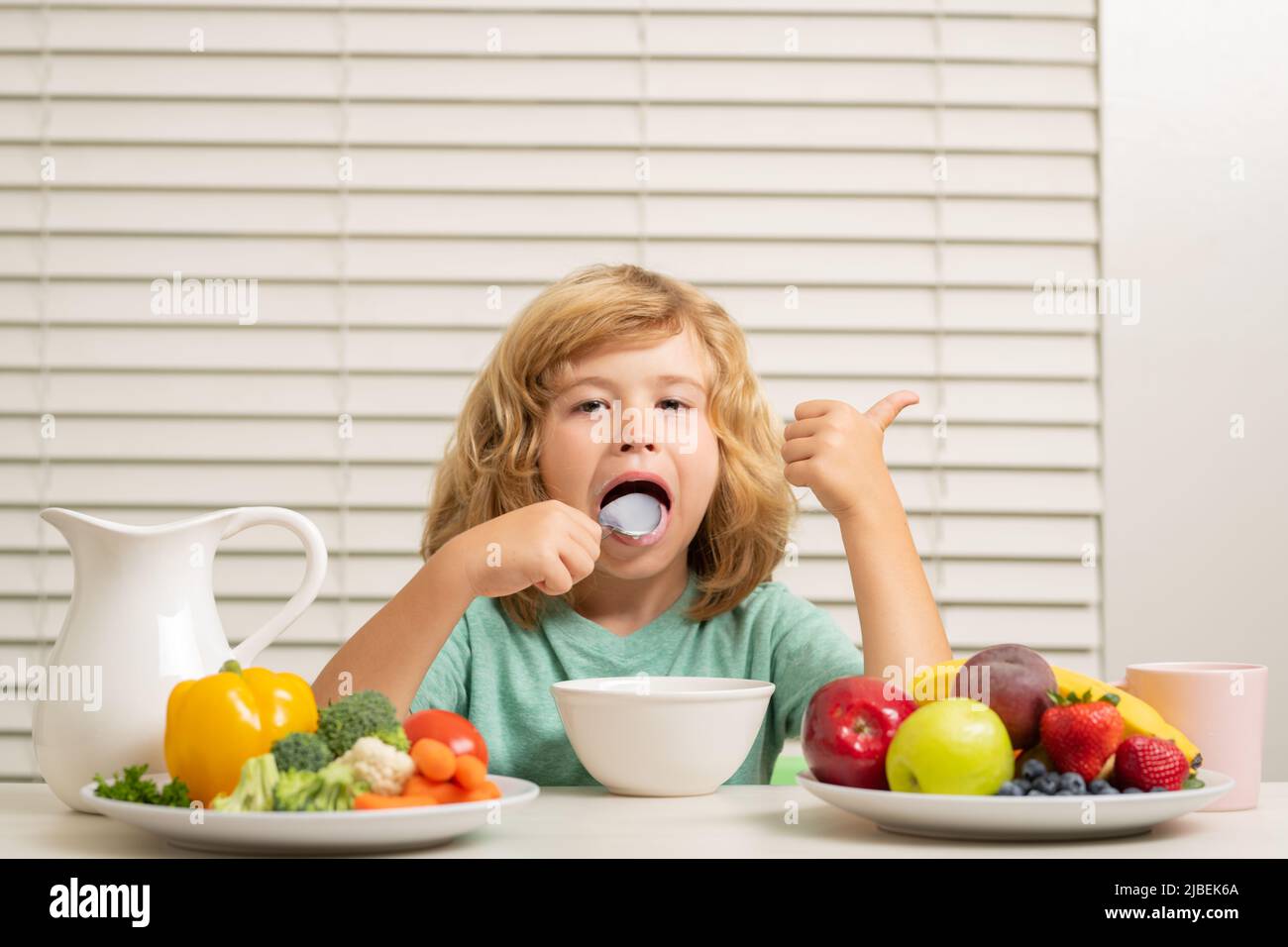 Kid preteen boy lick spoon in the kitchen at the table eating vegetable ...