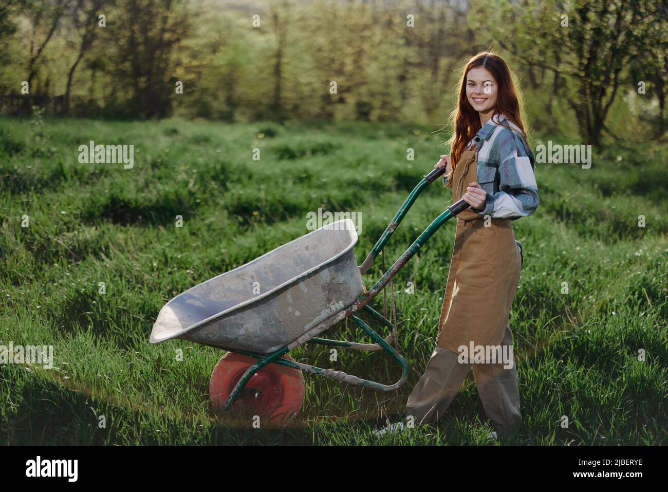 A happy woman with a cart works in her country home in the countryside against a backdrop of ...