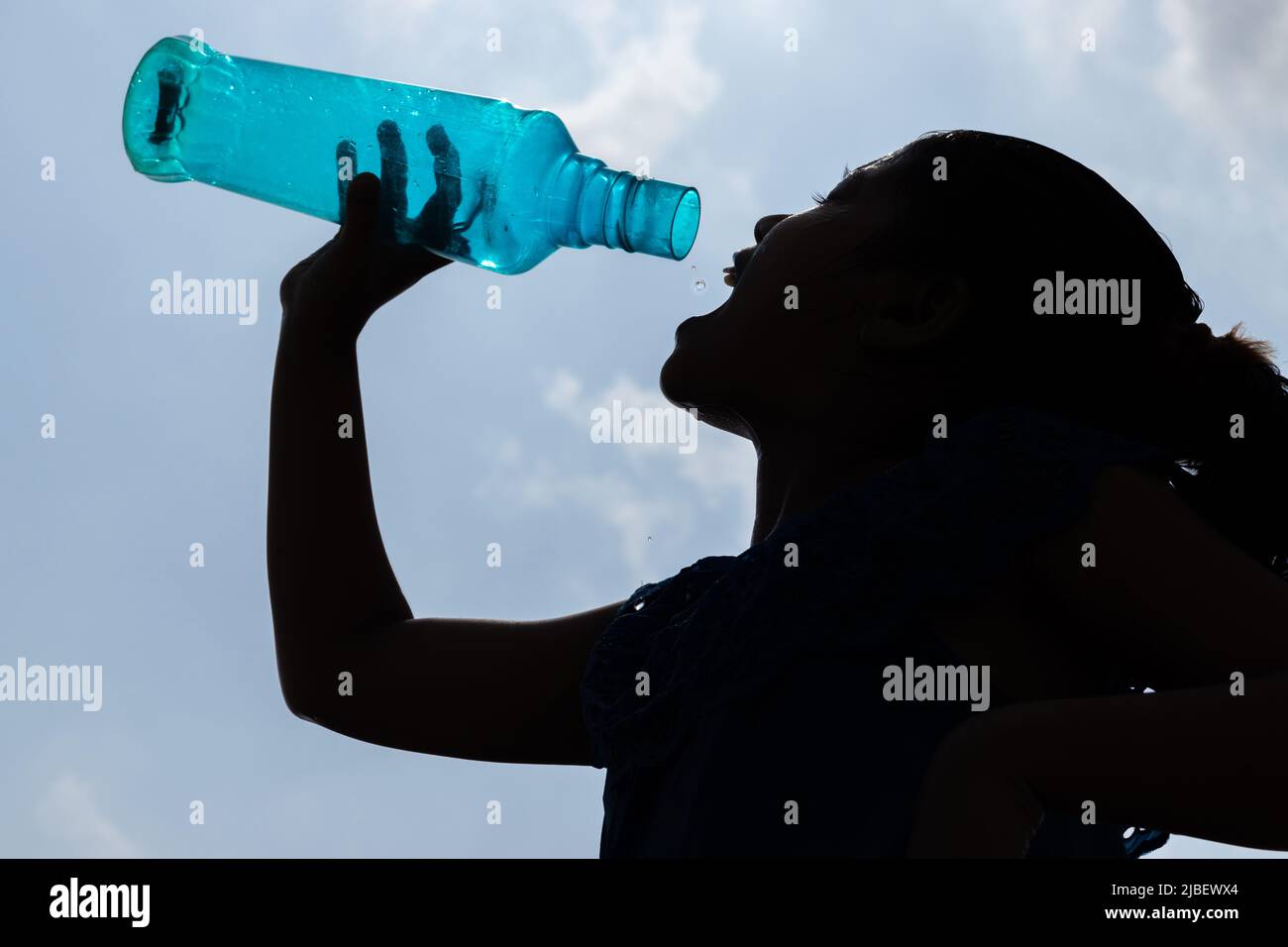 Silhouette of a girl drinking last drop of water from a empty blue ...