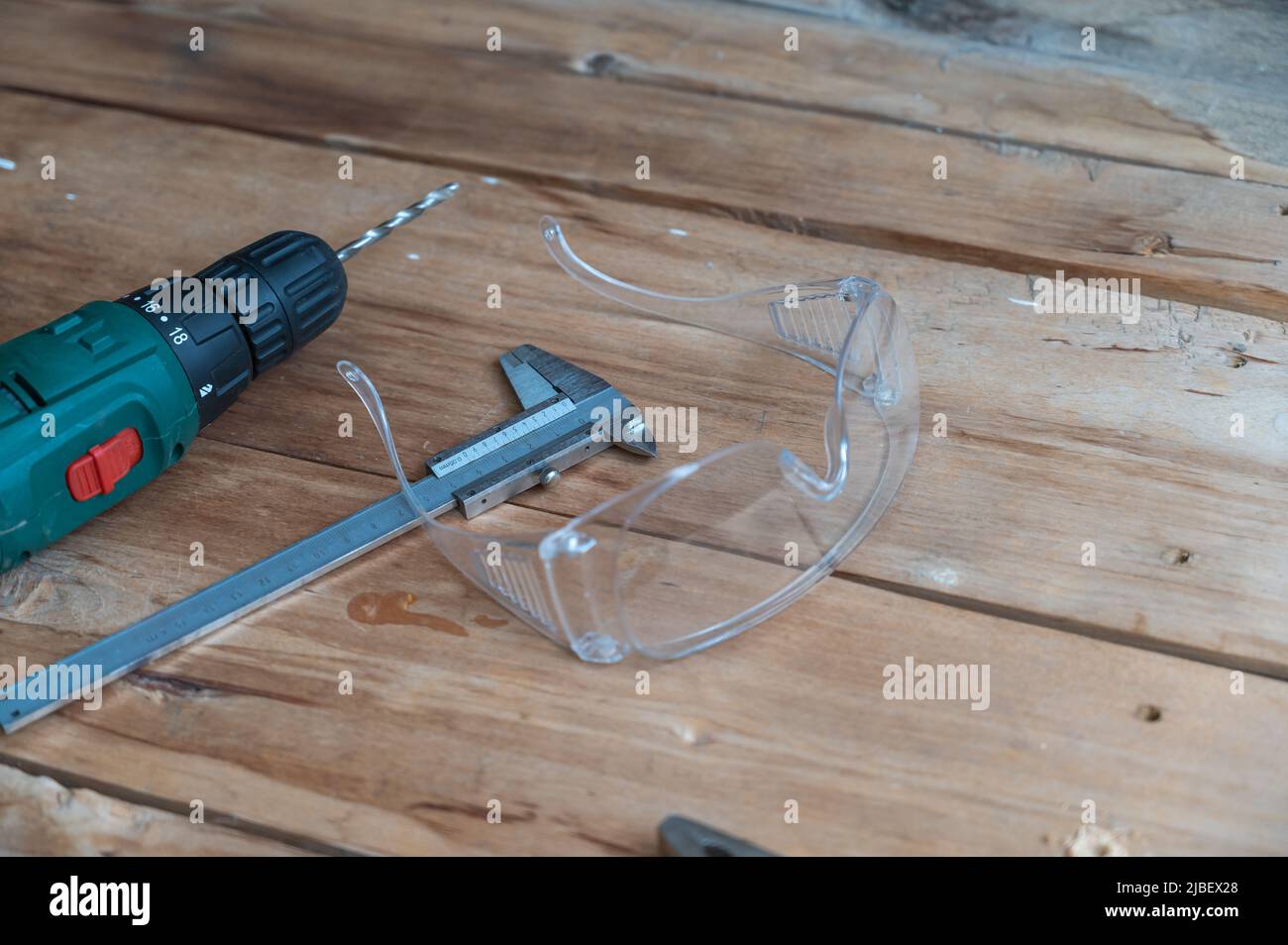 Electric drill, caliper, pliers and safety goggles lie on a wooden ...