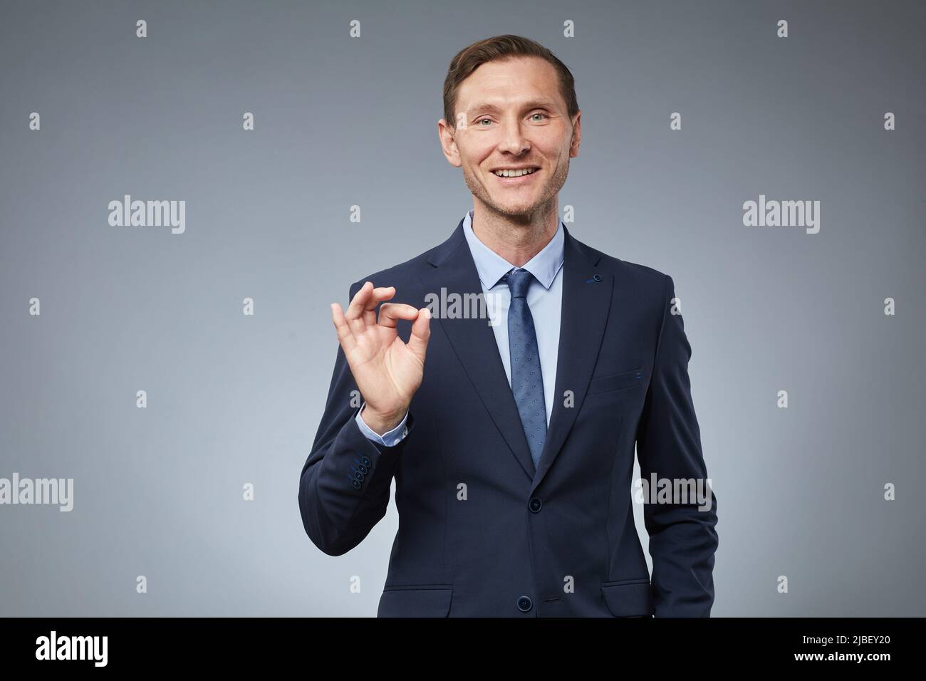 Waist up portrait of smiling Caucasian businessman showing OK sign ...
