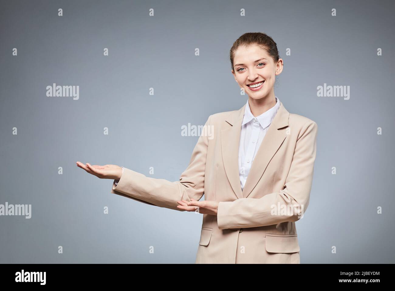 Waist up portrait of smiling young businesswoman pointing at copy space ...
