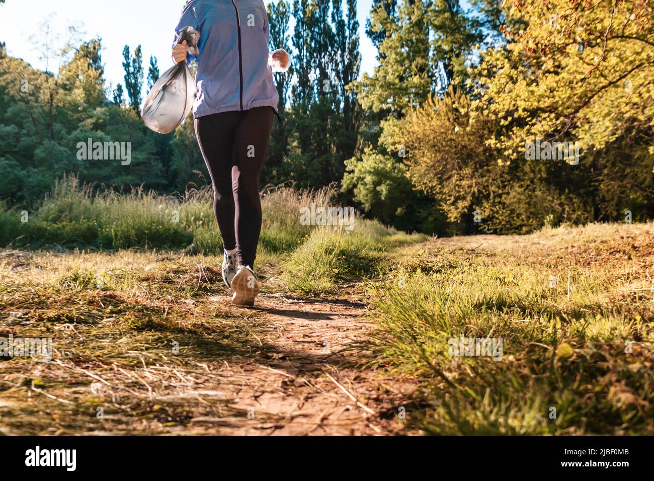 Plogging. Person in sportswear jogging at the park and holding a bag of ...