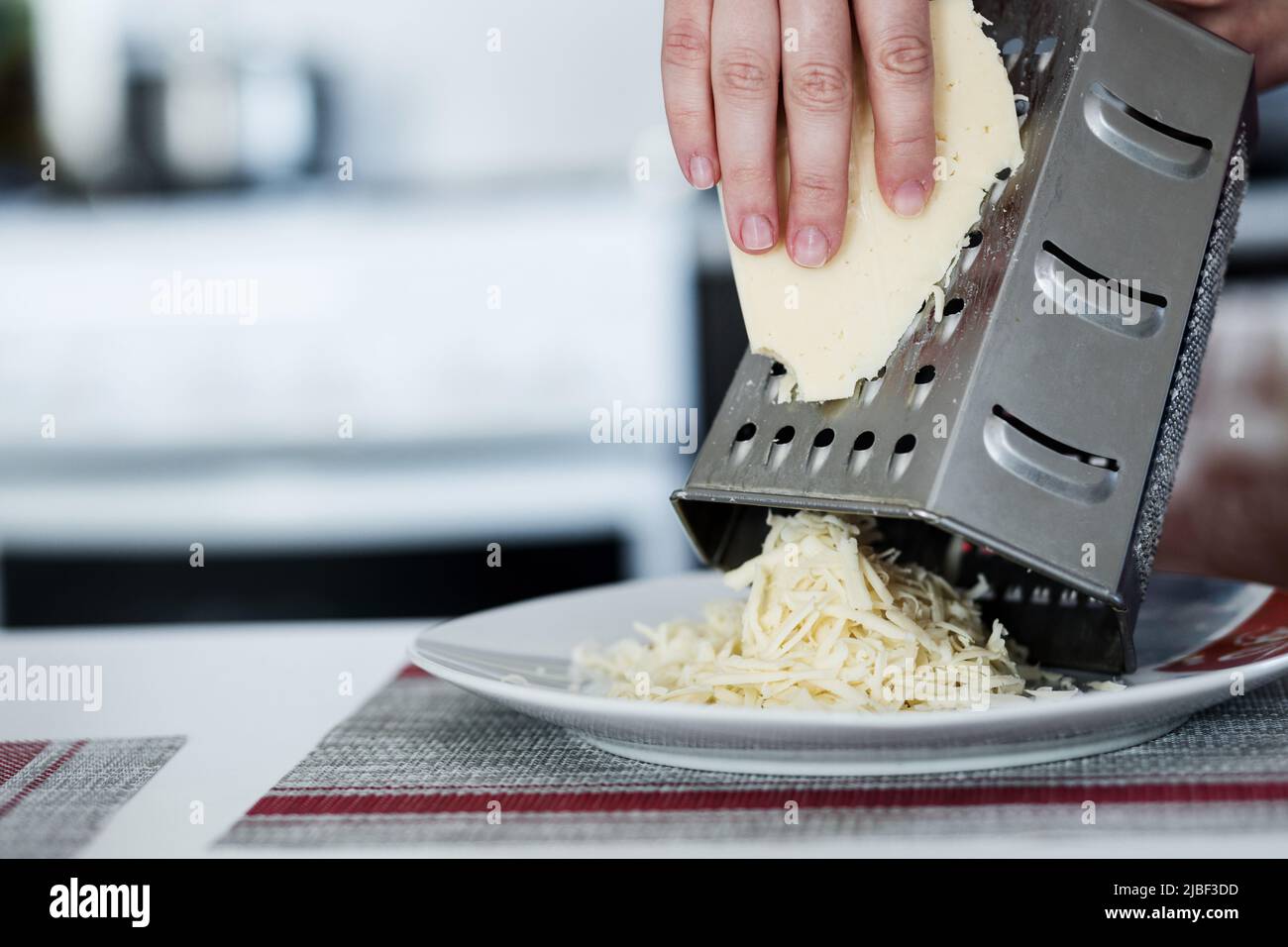 Woman grating cheese on kitchen table. cooking, food and home concept ...