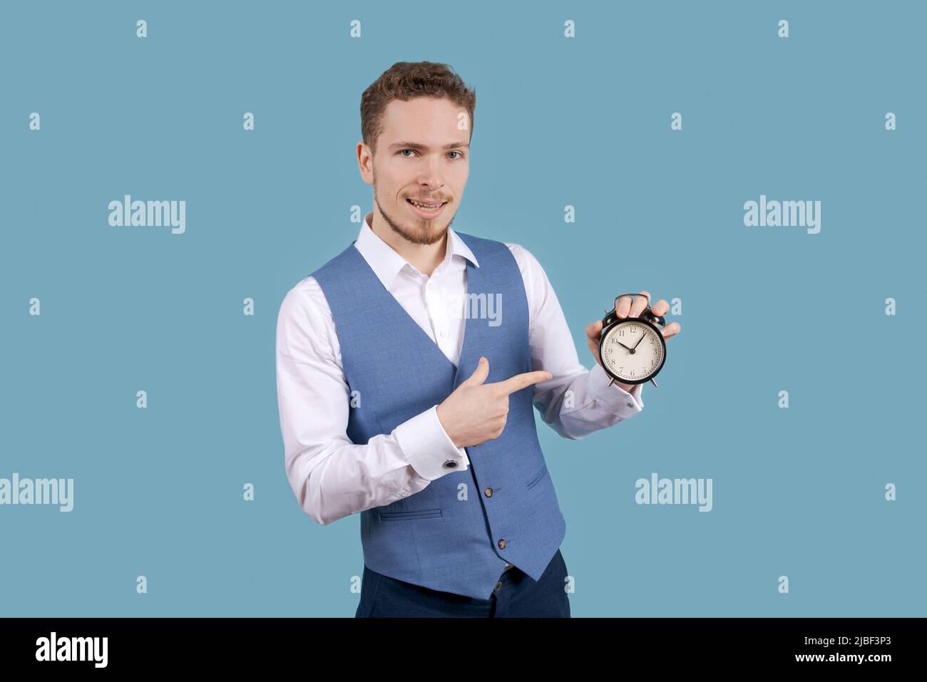 Young man in suit pointing at black alarm clock with his index finger ...