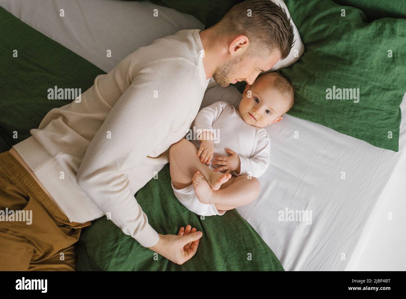 A handsome young dad lies in bed in the bedroom and hugs his loving ...