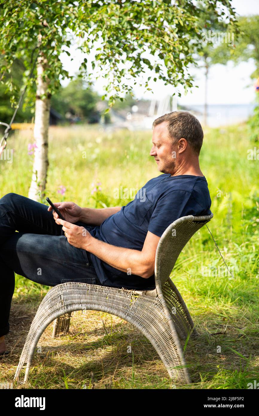 Man using smart phone while sitting in wicker chair Stock Photo - Alamy