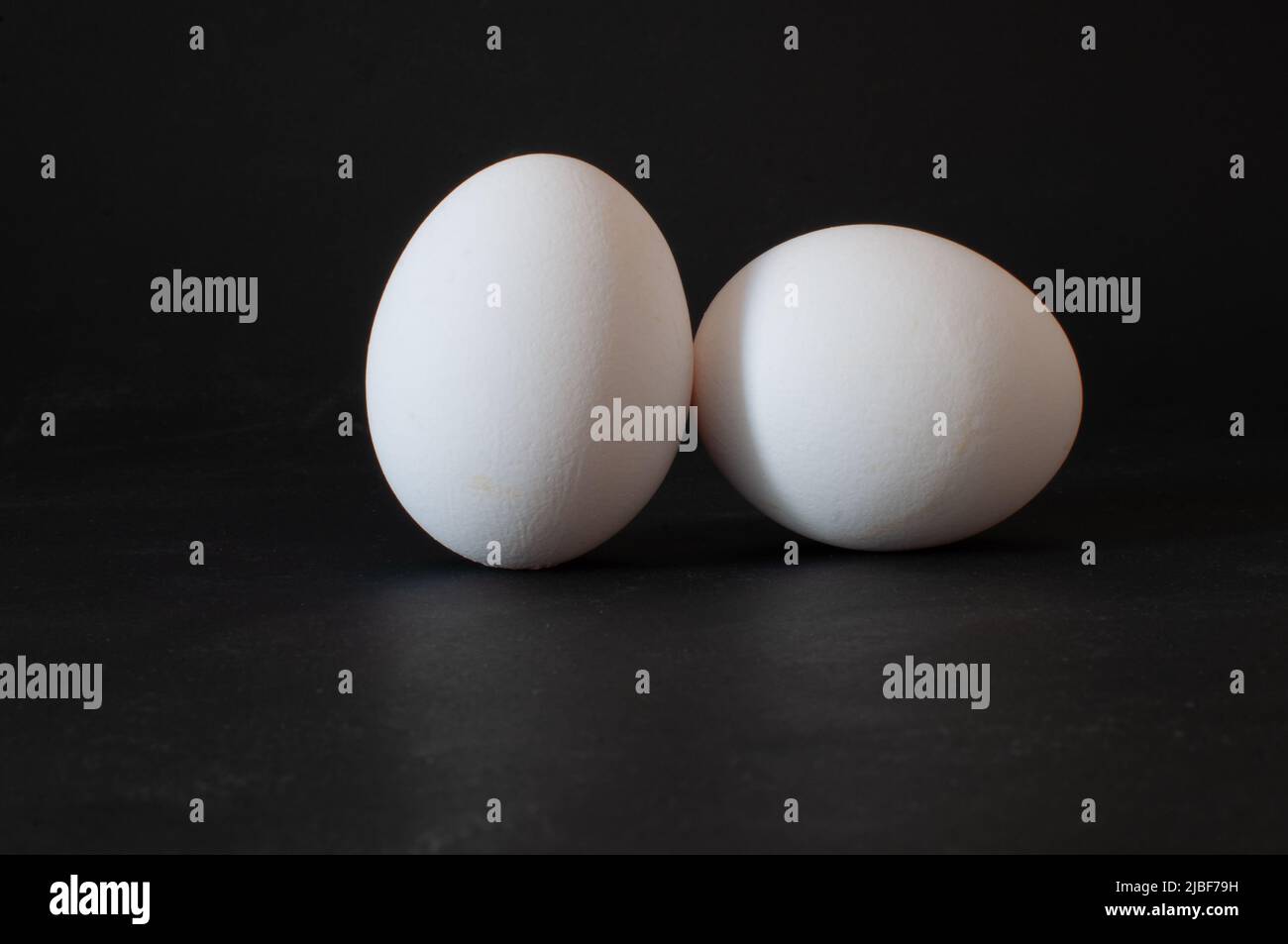 Two eggs, profile view of white raw chicken eggs isolated on dark ...