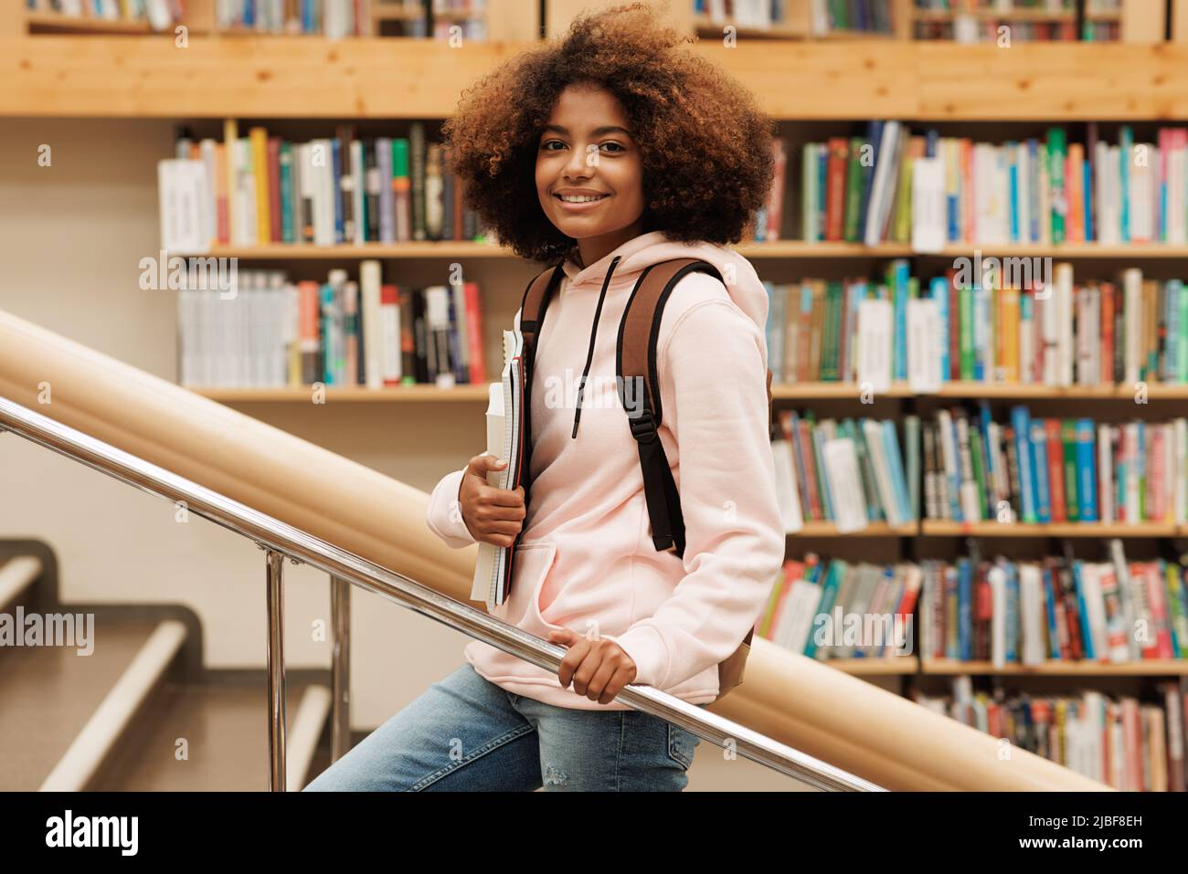 Beautiful girl with curly hair standing in library against bbokshelves ...