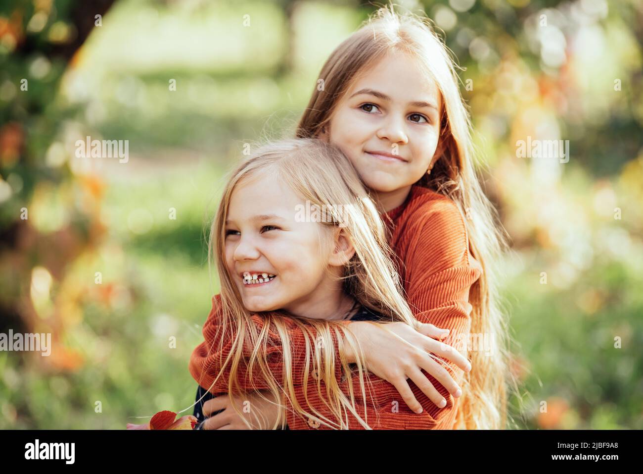 portrait of two happy sisters laughing hugging each other on warm and ...