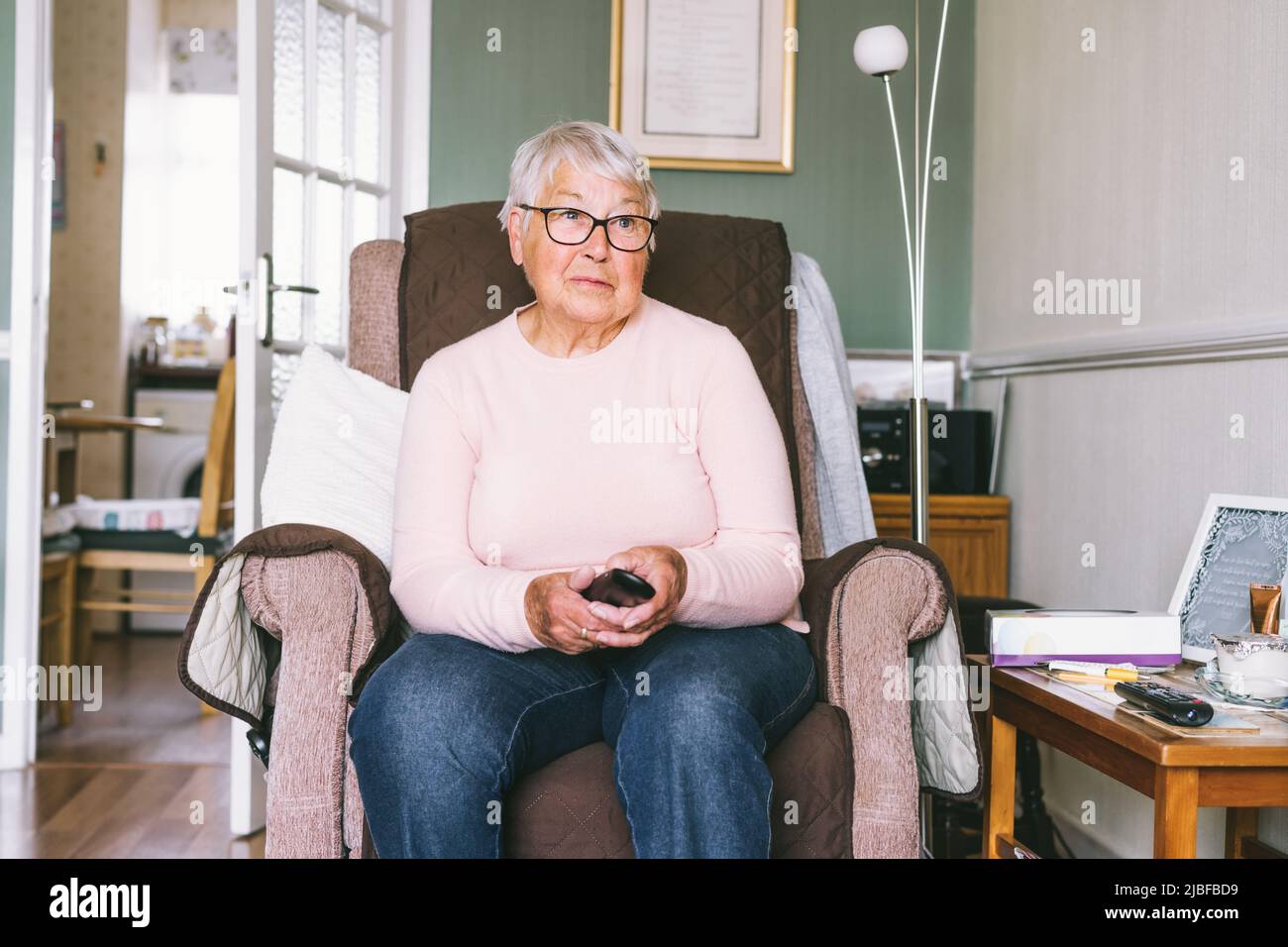 Portrait of retired elderly woman in comfortable armchair with TV ...