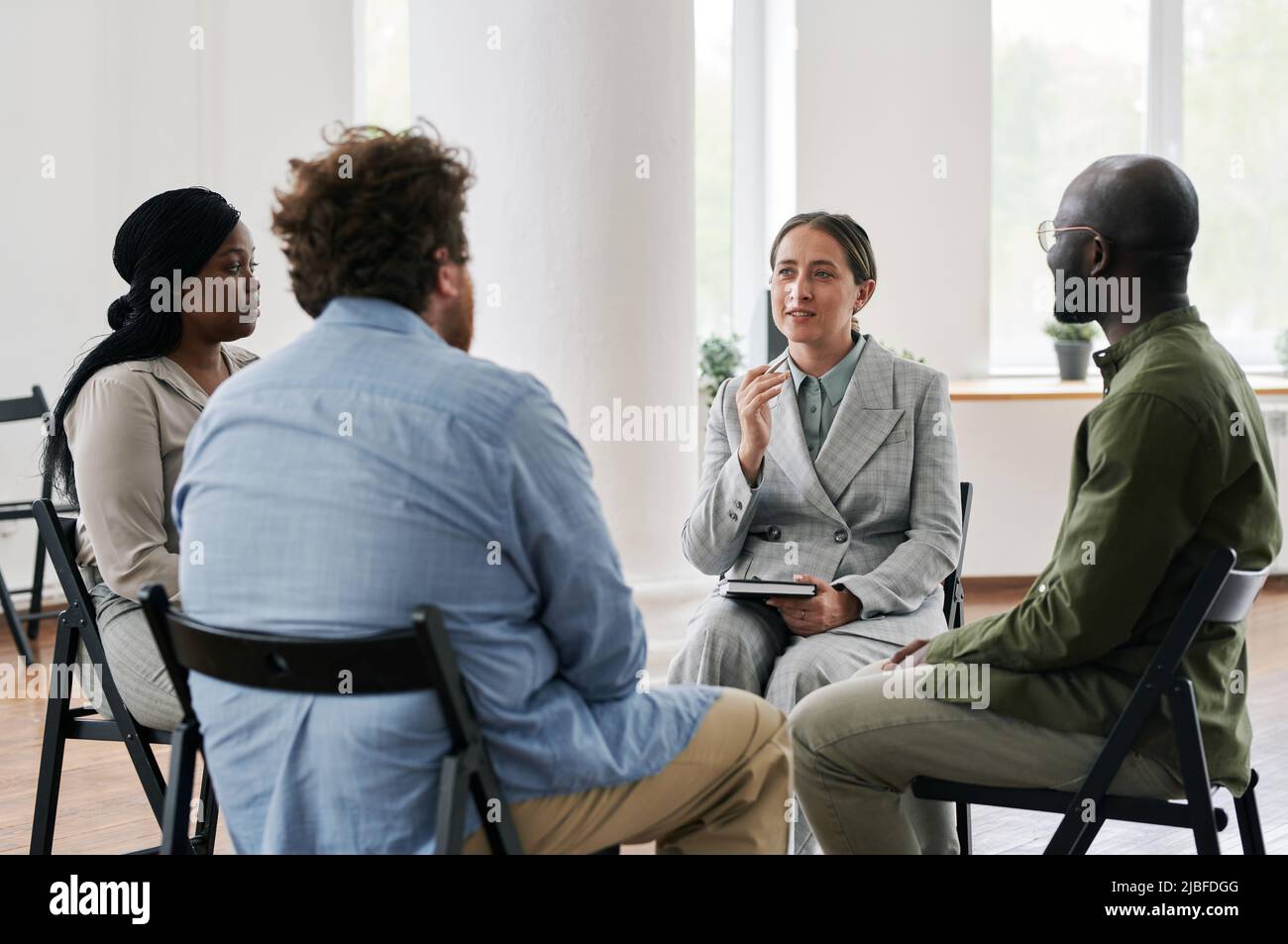 Young confident female psychologist in suit talking to group of ...