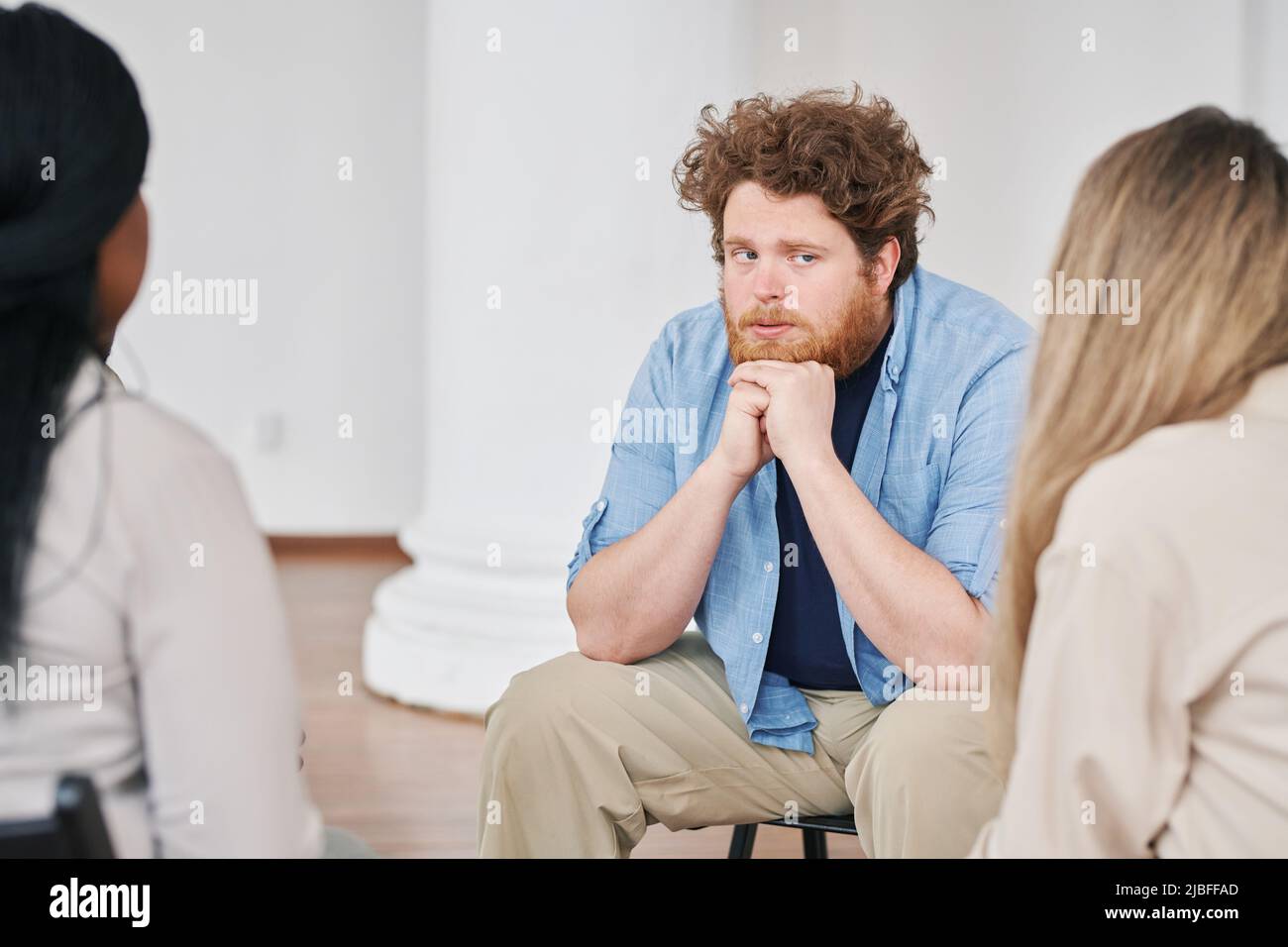 Sad young man in casualwear looking at counselor during session while ...