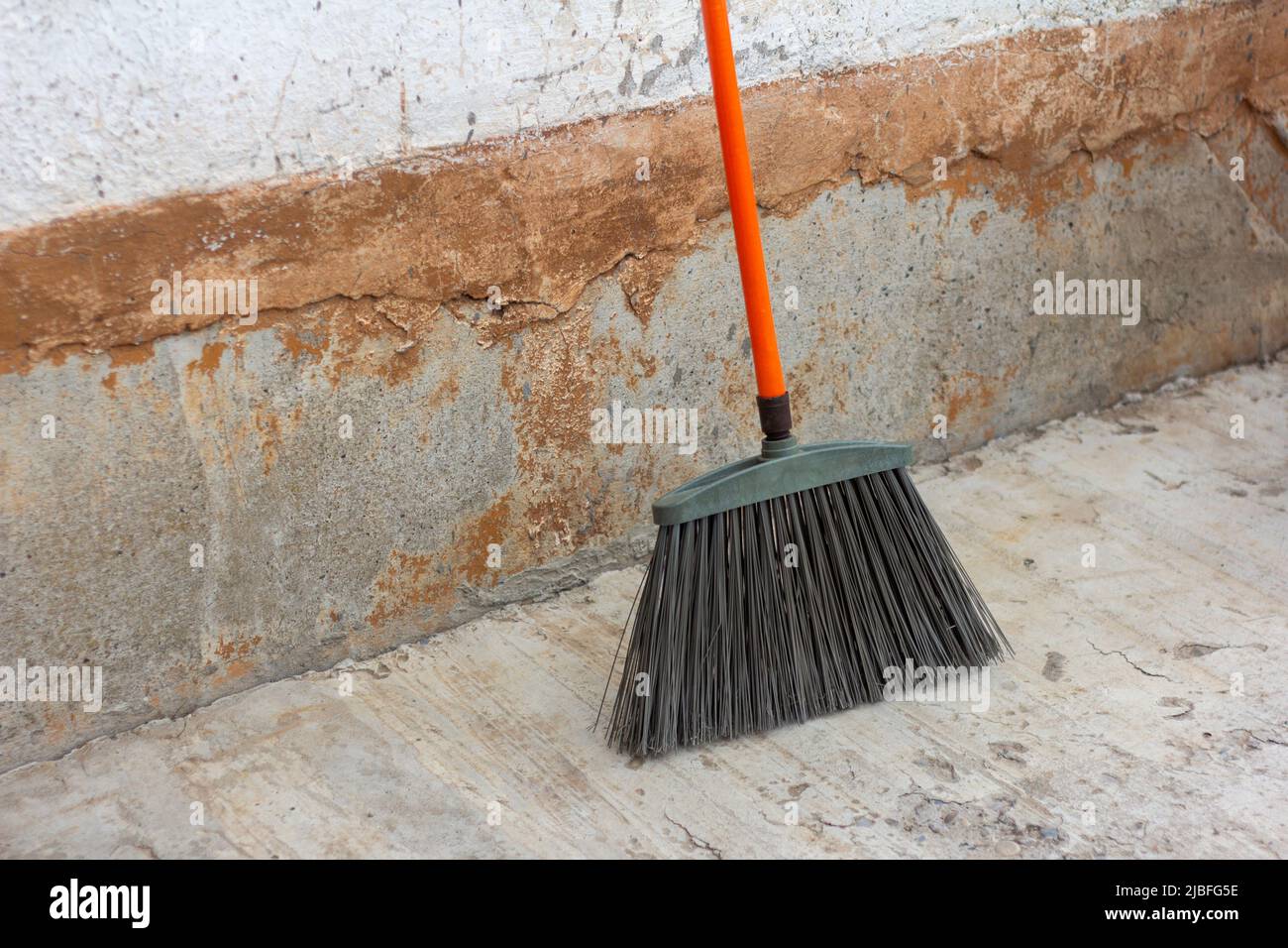 A large street cleaning broom stands against a concrete wall on the ...