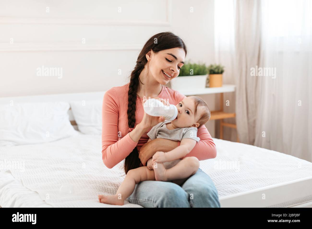 Baby care. Caring mother giving bottle with milk to her infant child ...