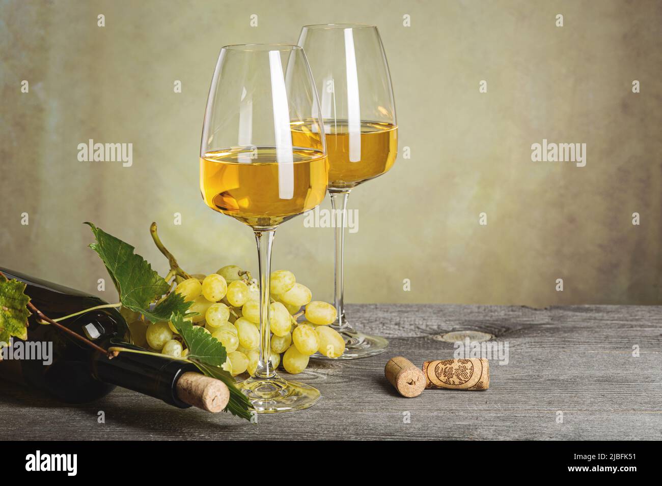 White wine in glasses, wine bottle and grapes on an old wooden table ...