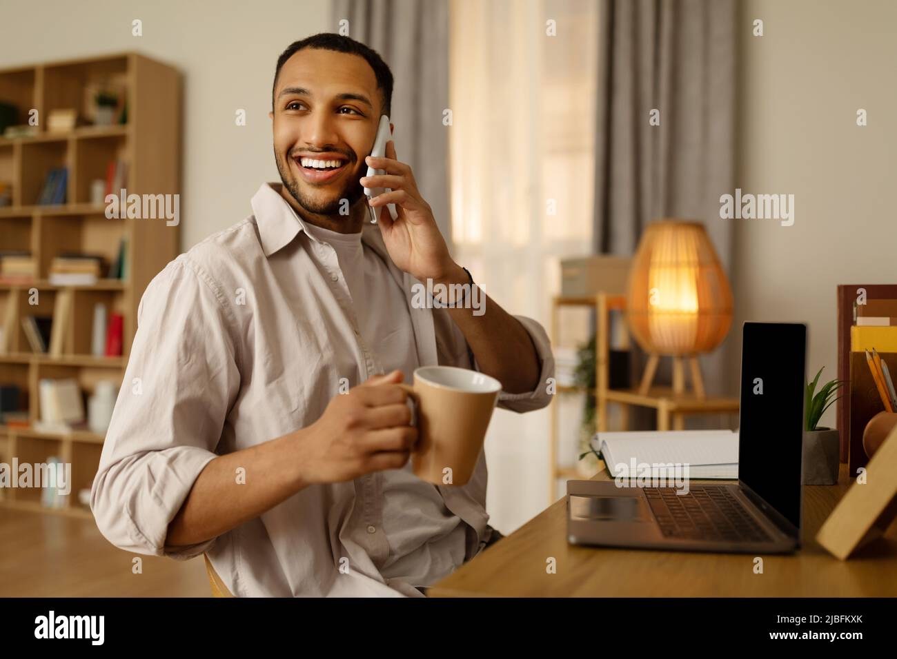 Positive young African American man with coffee talking on cellphone ...