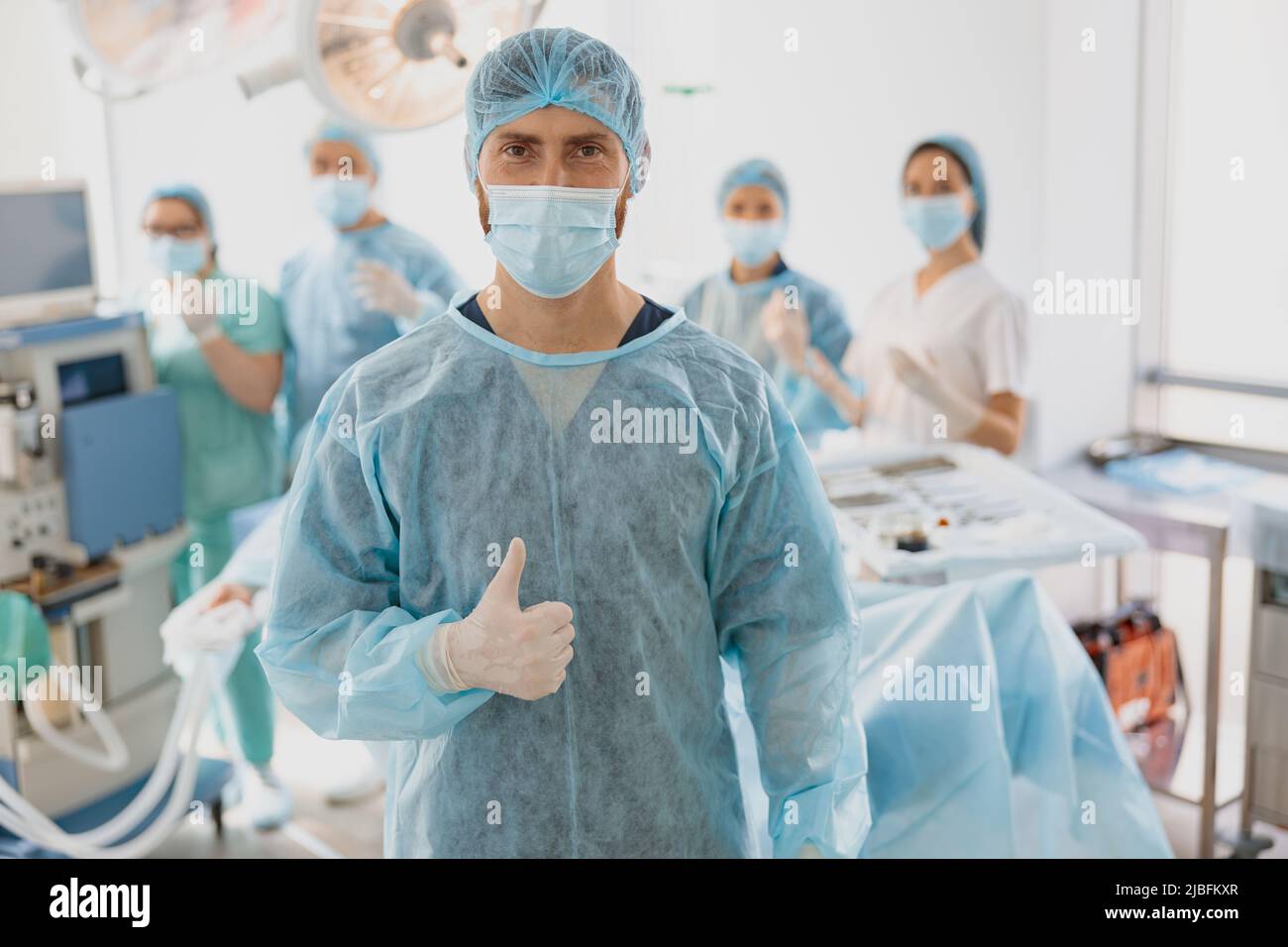 Portrait of surgeon standing in operating room and showing thumb up ...