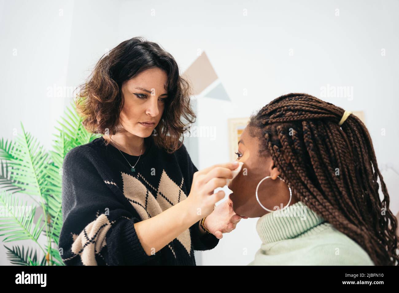 Focused female visagiste using sponge to smear foundation on cheek of ...