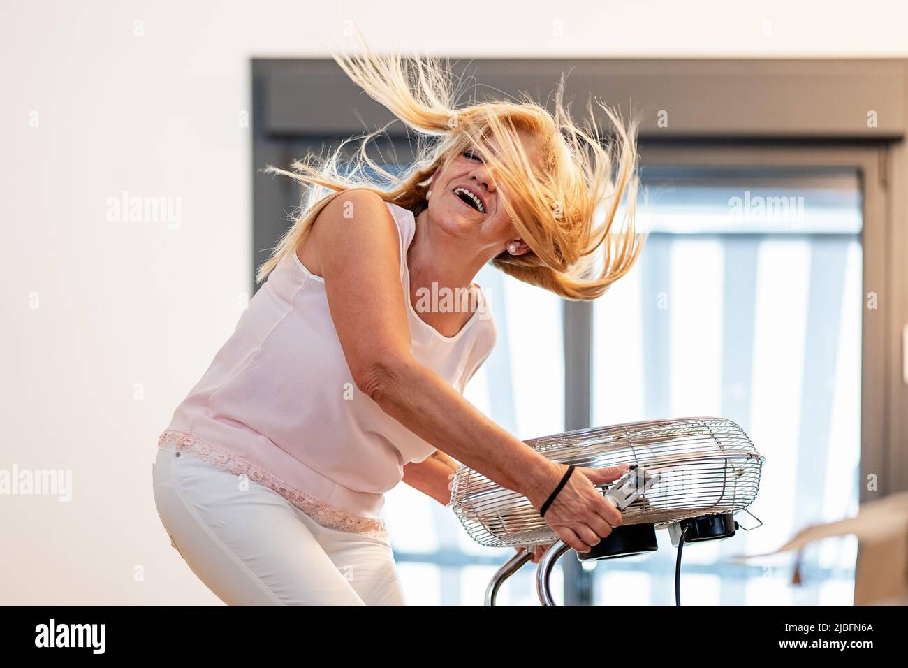 Cheerful blond mature Woman at home standing in living room playing ...