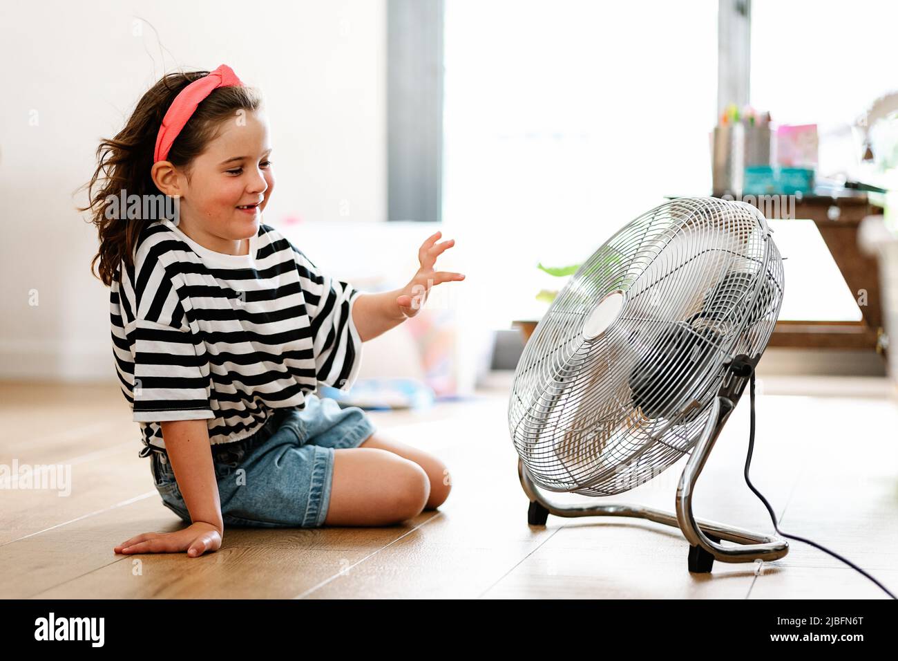Little girl at home sitting on the floor playing with fan Stock Photo ...