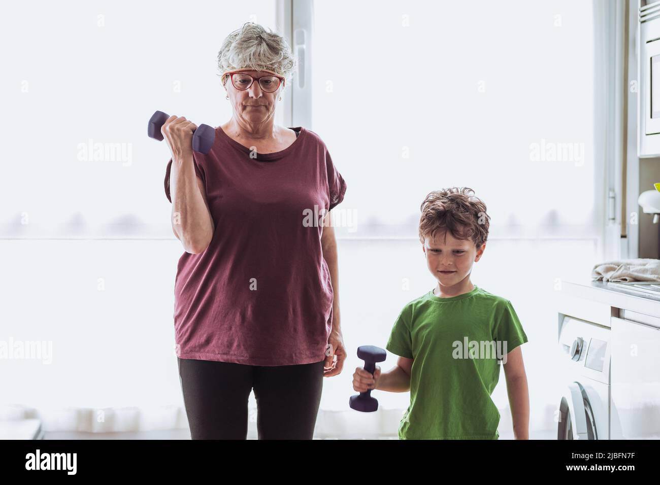Grandma and grandchild in activewear doing exercise with dumbbells ...