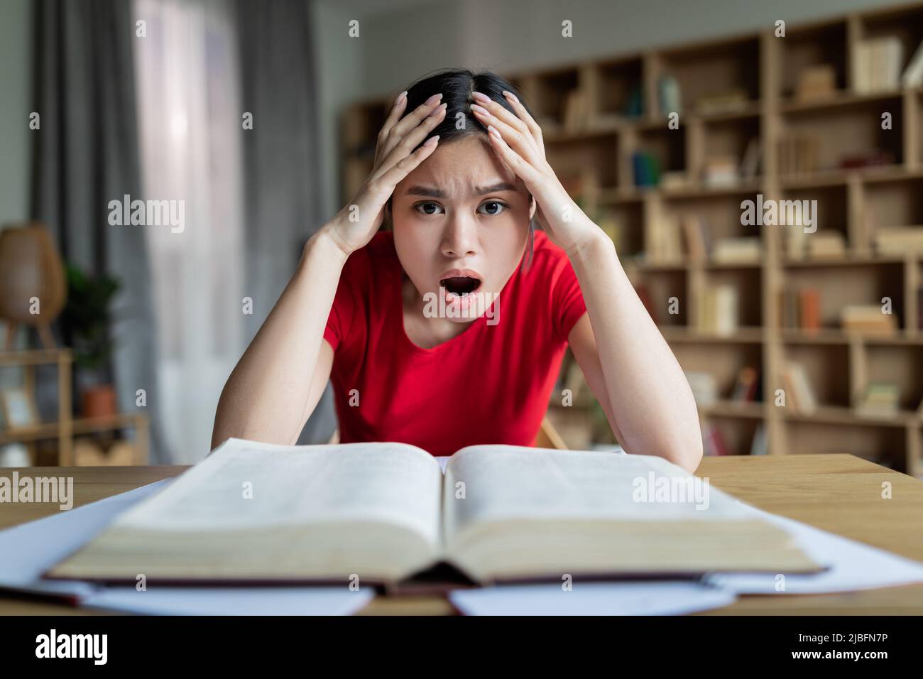 Sad shocked teen chinese lady student with open mouth study at table ...