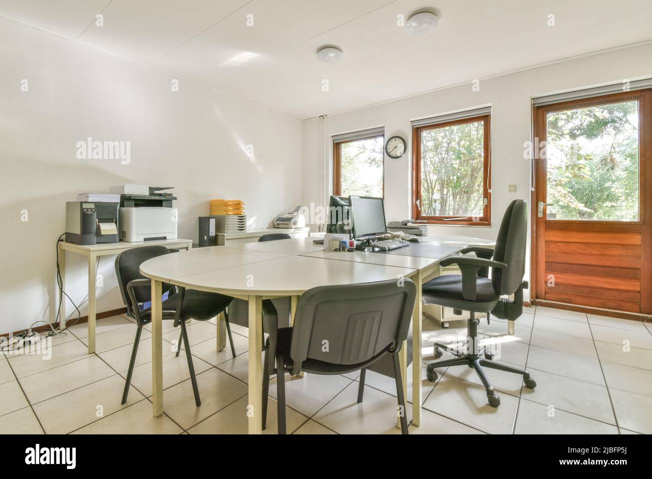 Tables with modern computers and printers in spacious office with ...