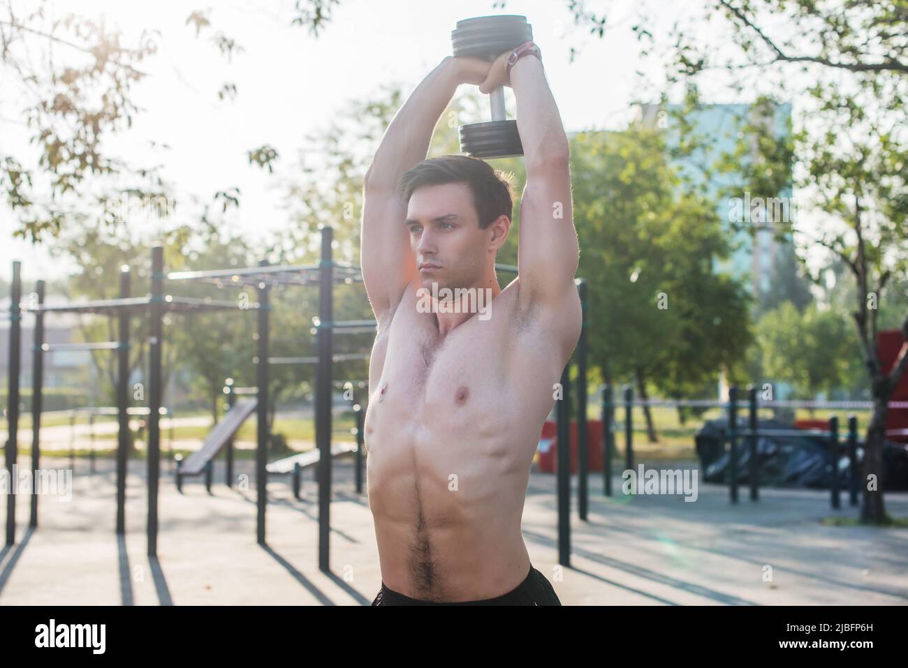 Muscular male athlete with arms raised doing lifting exercises with ...
